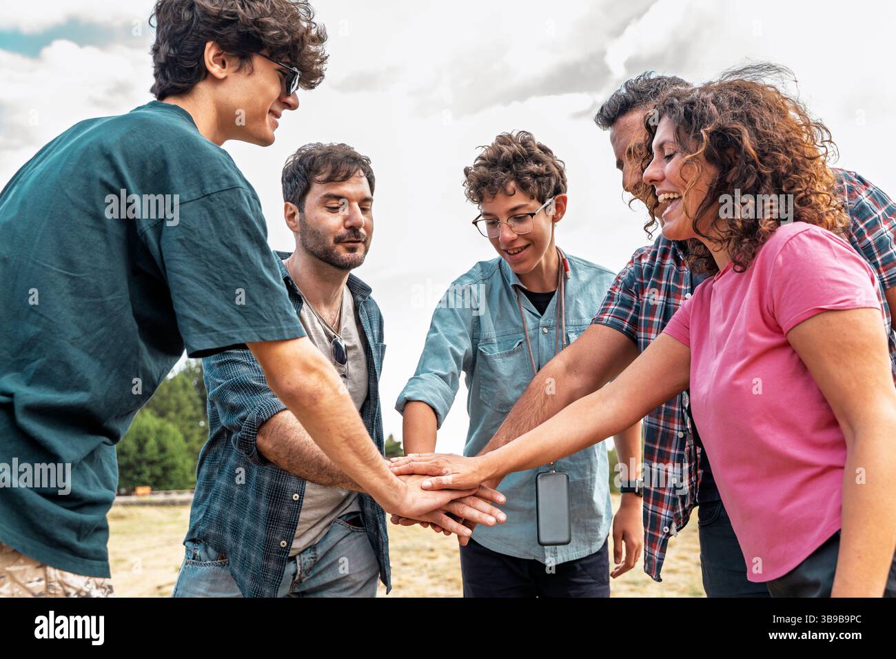 A diverse group of friends joining hands in a teamwork gesture ...