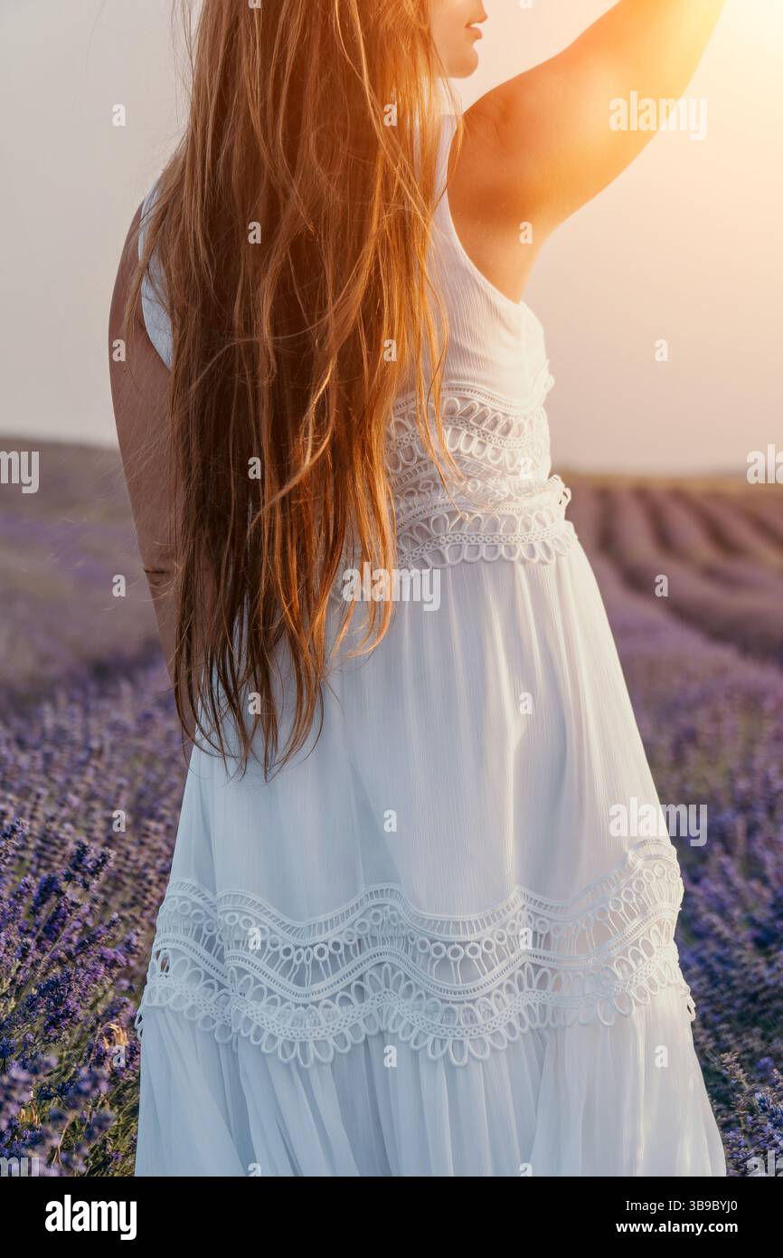 Woman in white dress stands in a lavender field, long hair flowing, arm ...