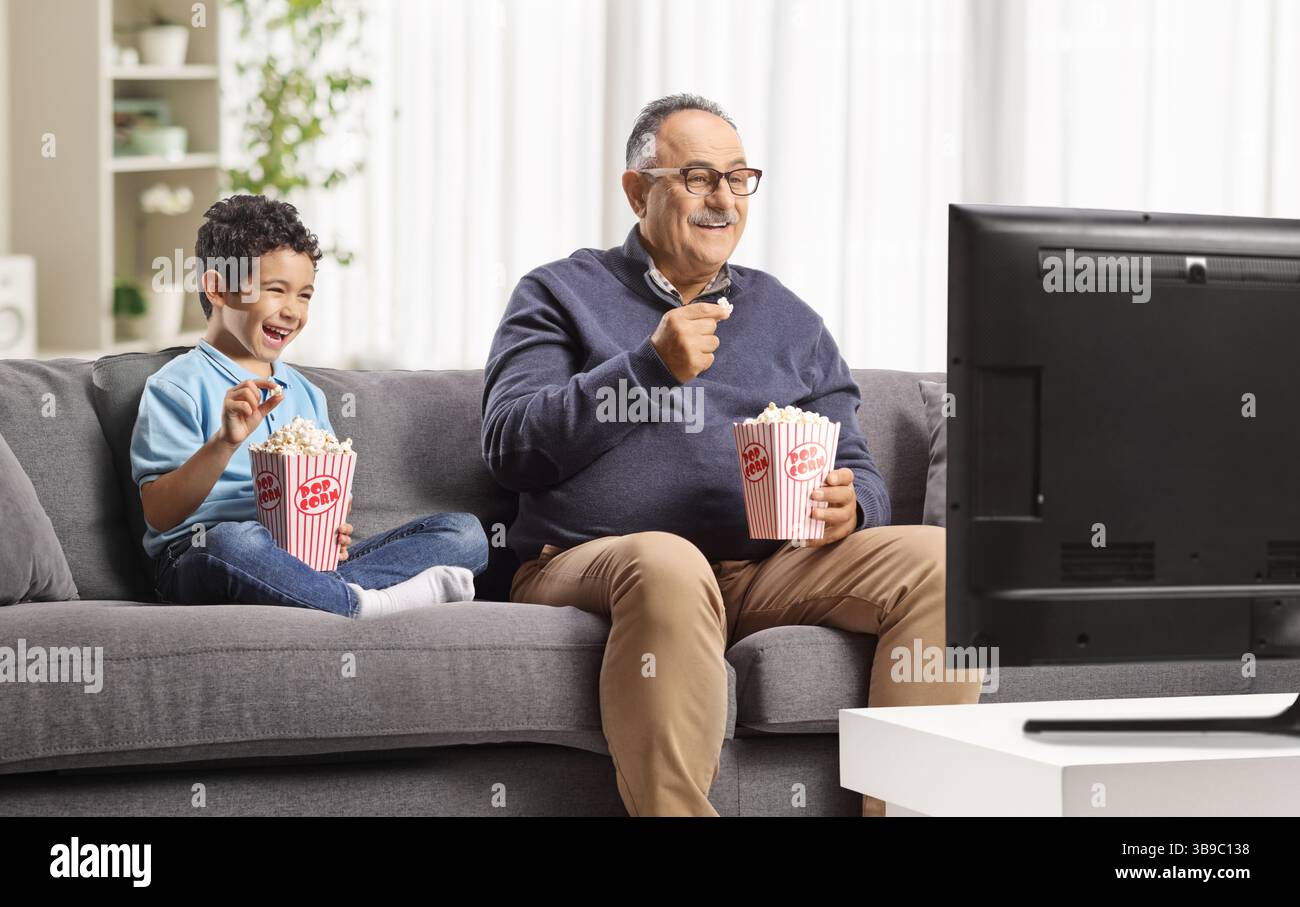 Mature man and a kid watching tv and eating popcorn isolated on white ...