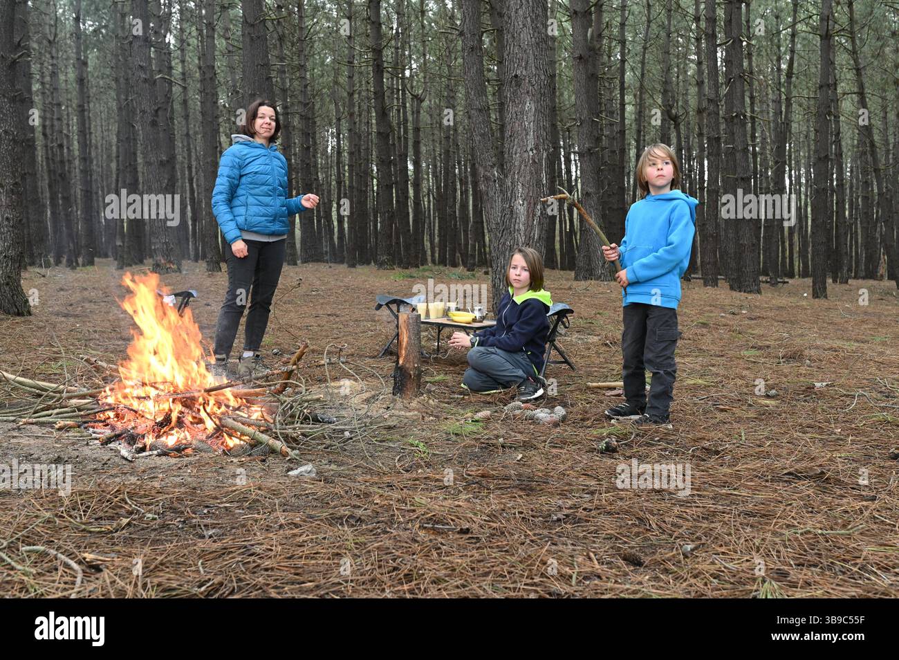 Mother and two children sit by a campfire in the forest, eating and ...