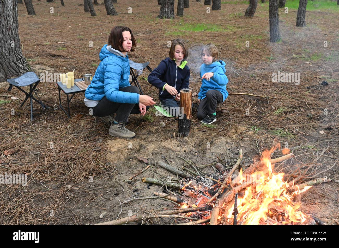 Mother and two children sit by a campfire in the forest, eating and ...