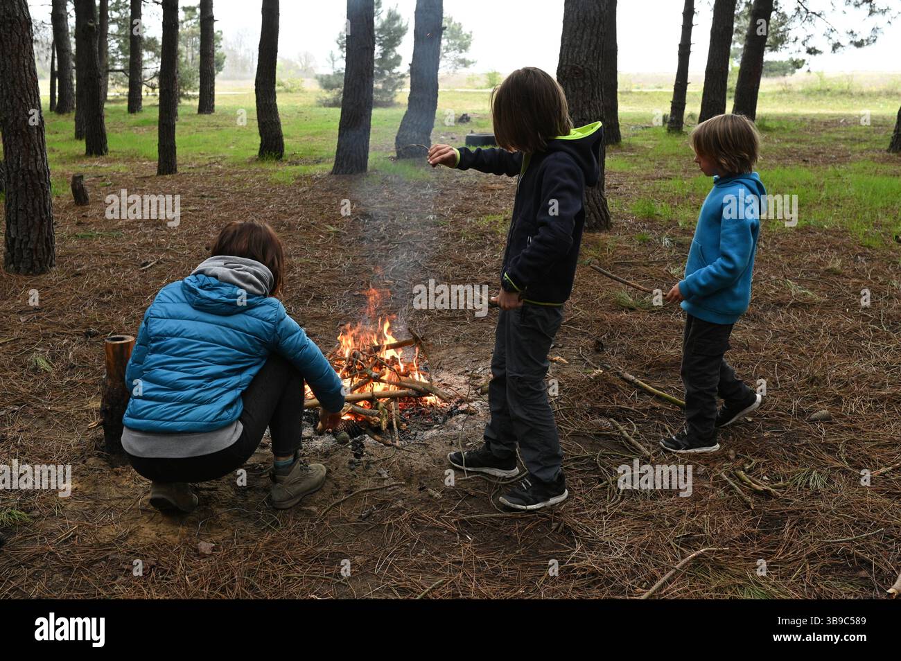Mother and two children sit by a campfire in the forest, eating and ...
