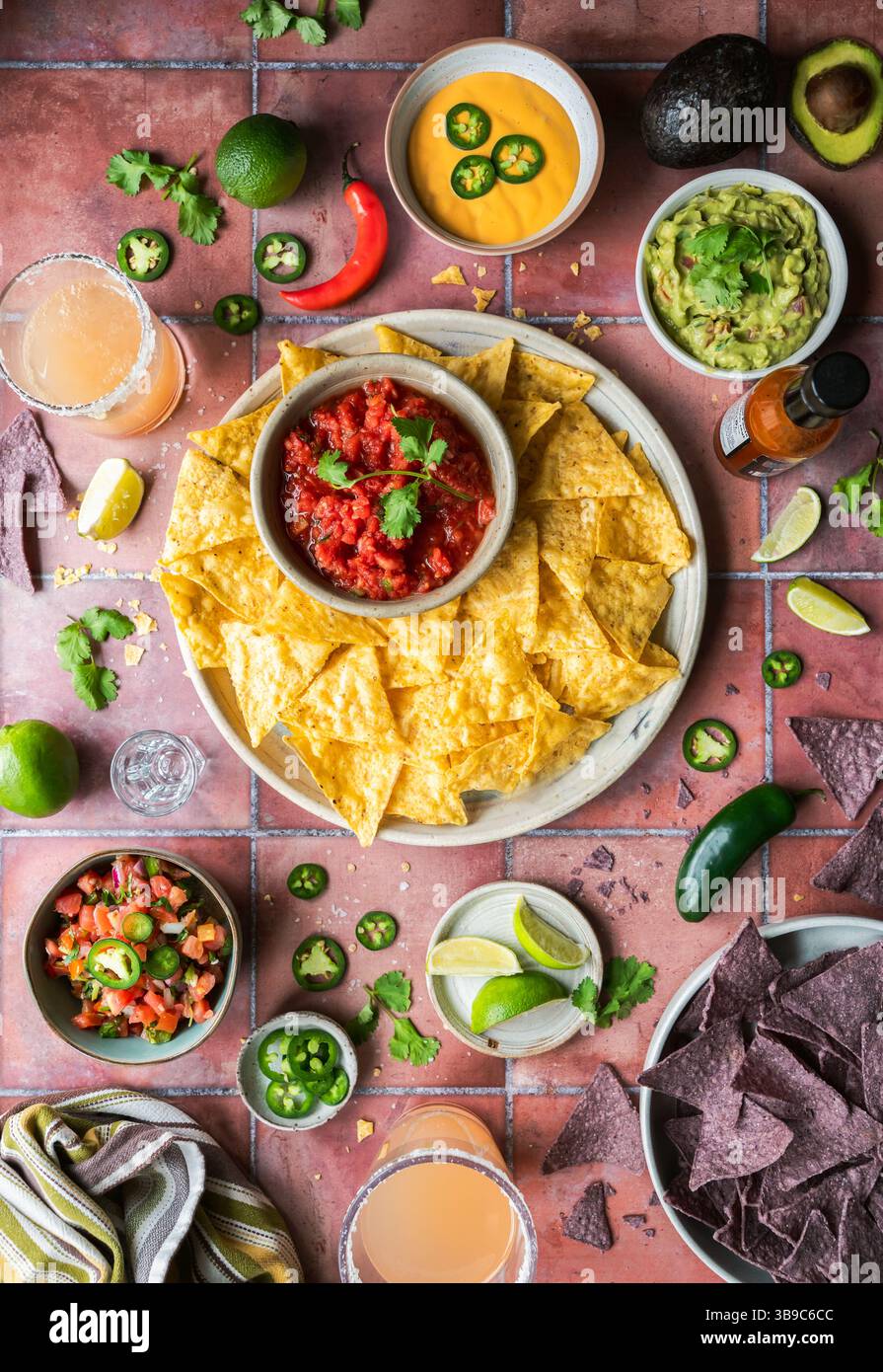 Top view tortilla chips, salsa, guacamole, queso and drinks on tile ...