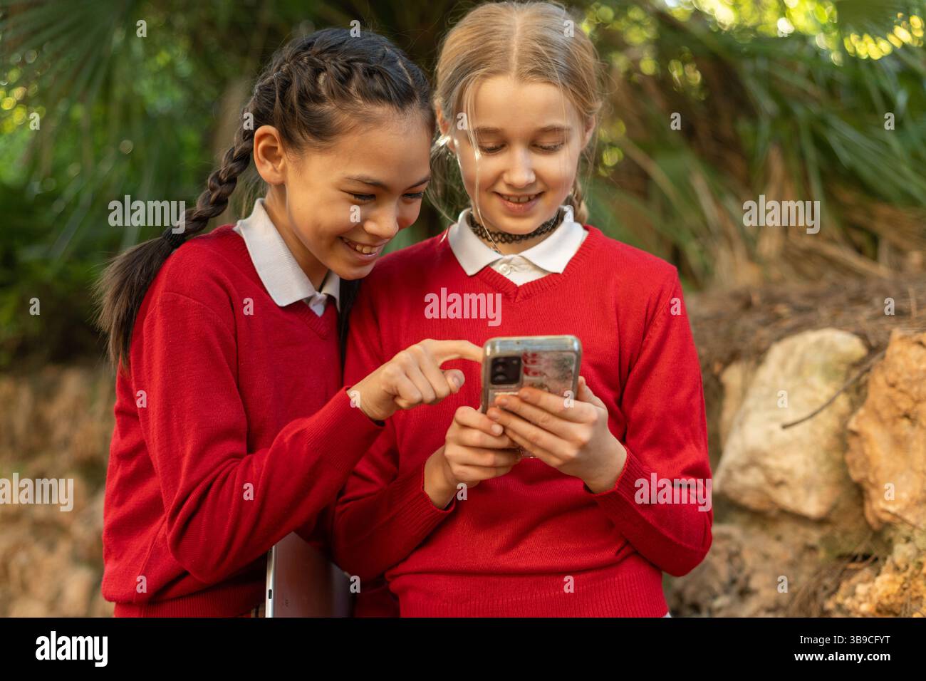 Two smiling students using smartphone in school garden Stock Photo - Alamy