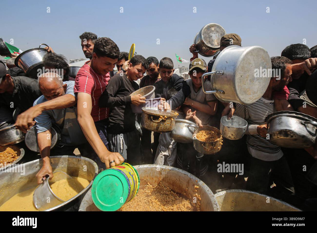 Palestinians wait in long queues to receive pots of food distributed by ...