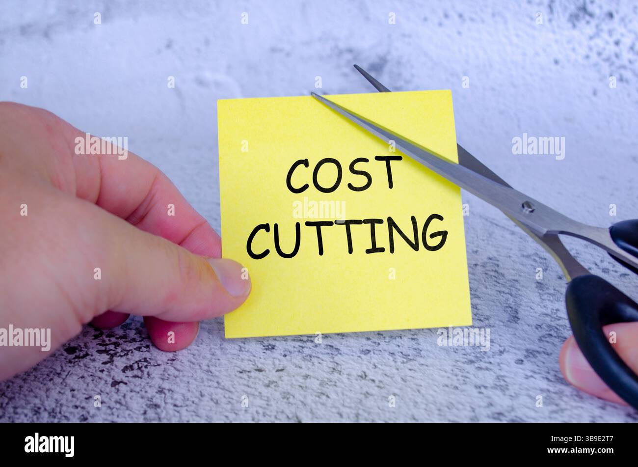 Hand holding a yellow sticky note with the words Cost Cutting written ...