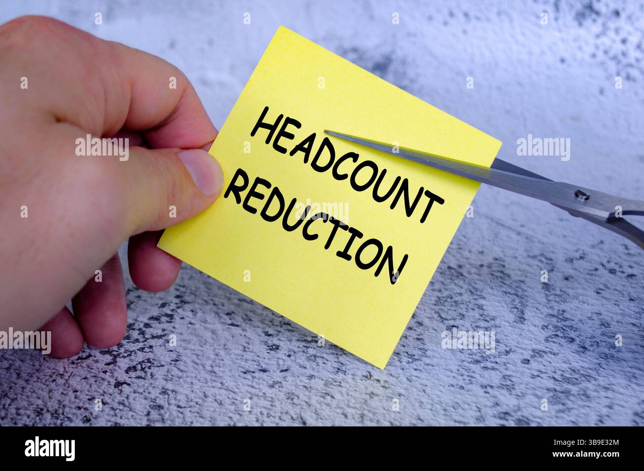 Hand holding a yellow sticky note with the words Headcount Reduction ...