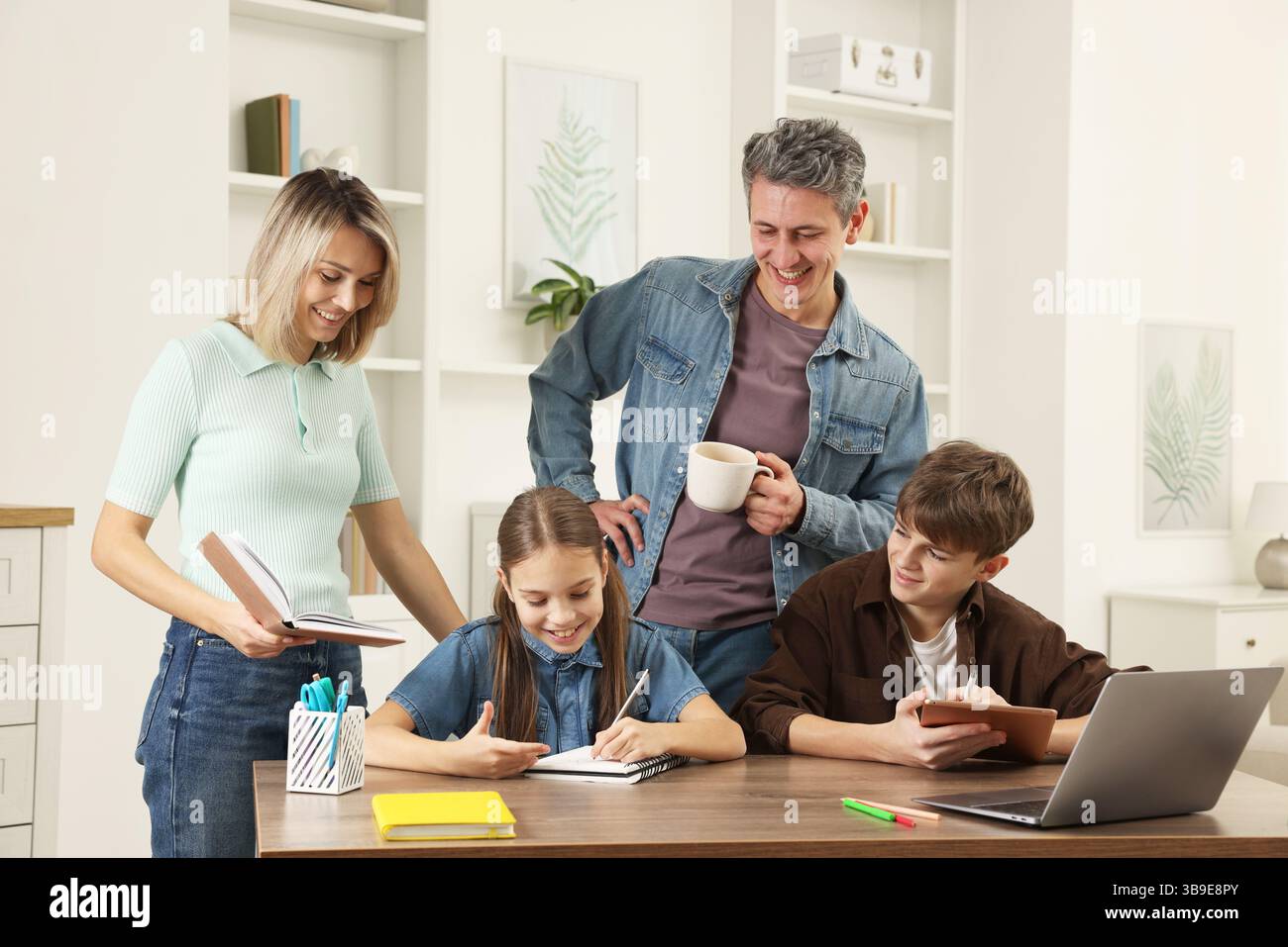 Happy parents and their children doing homework with laptop at table ...
