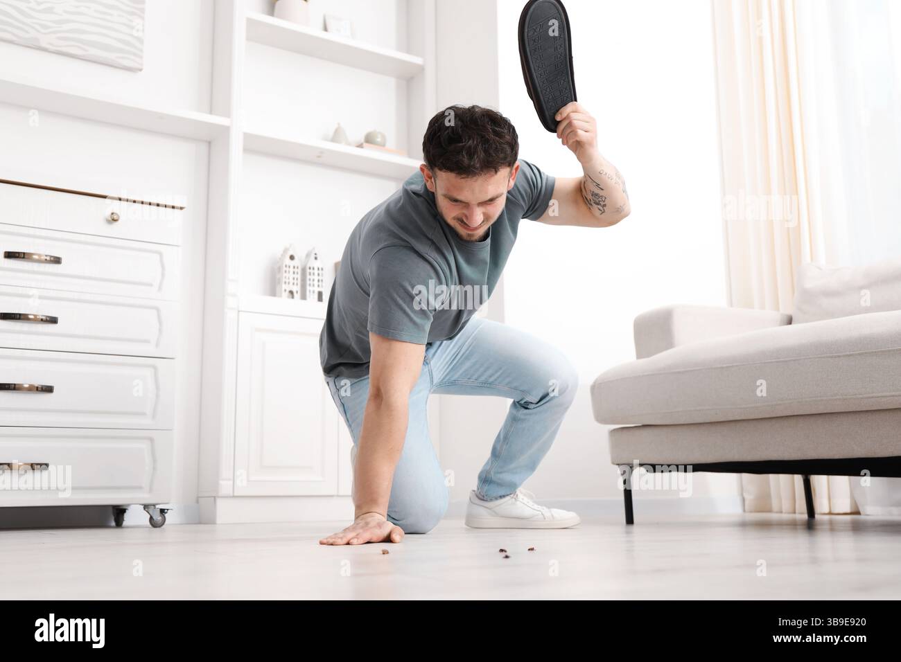 Emotional young man killing cockroaches with slipper on floor indoors ...