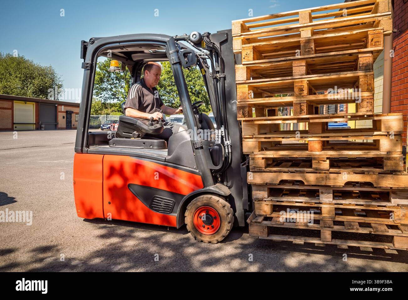 A man is driving a forklift with a stack of wood pallets on it. The ...