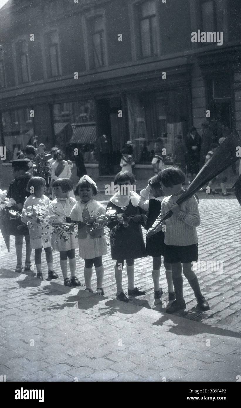 1930s, historical, young children line-up on a clobbed street to take ...