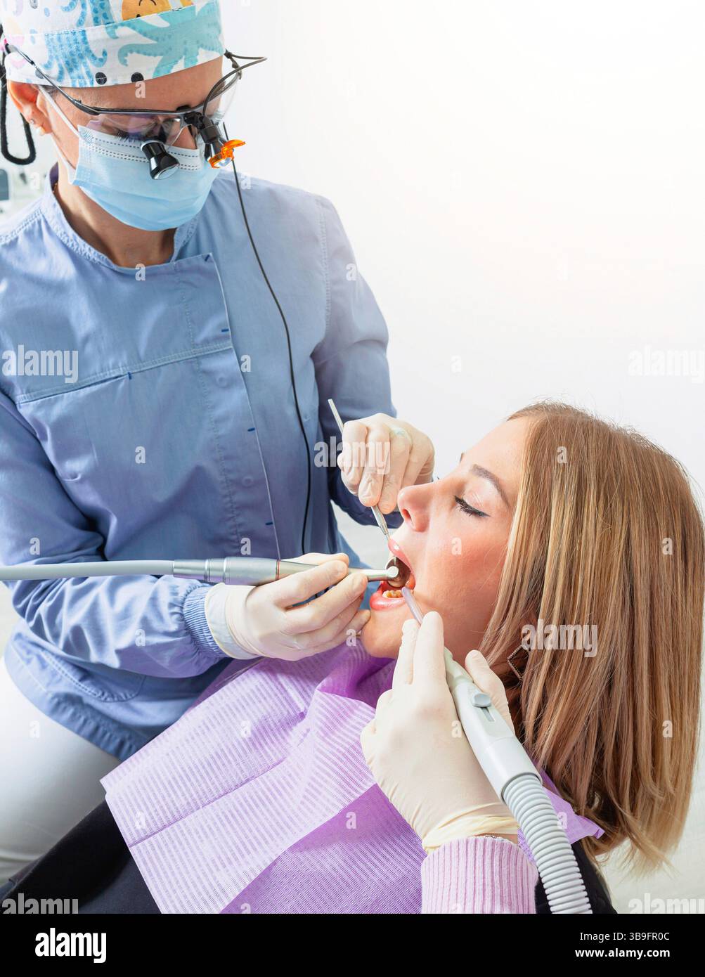 Dentist wearing magnifying glasses operating on patient's teeth using ...