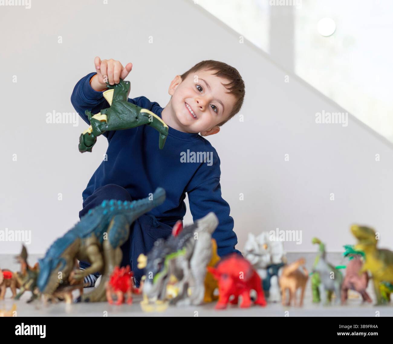 Smiling preschooler playing with a collection of plastic dinosaur toys ...