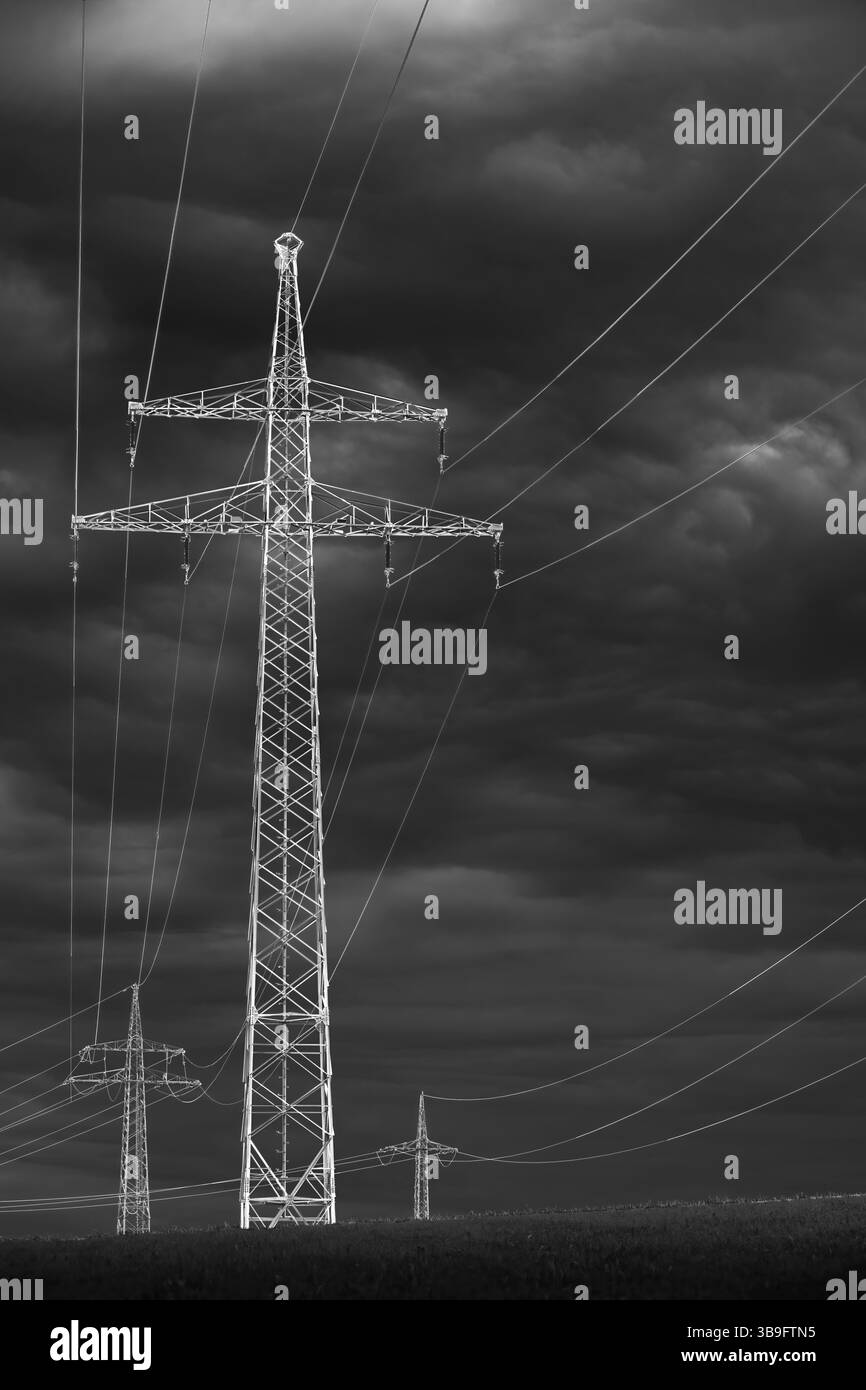 High-voltage pylons with cables under a dramatic sky in black and white ...