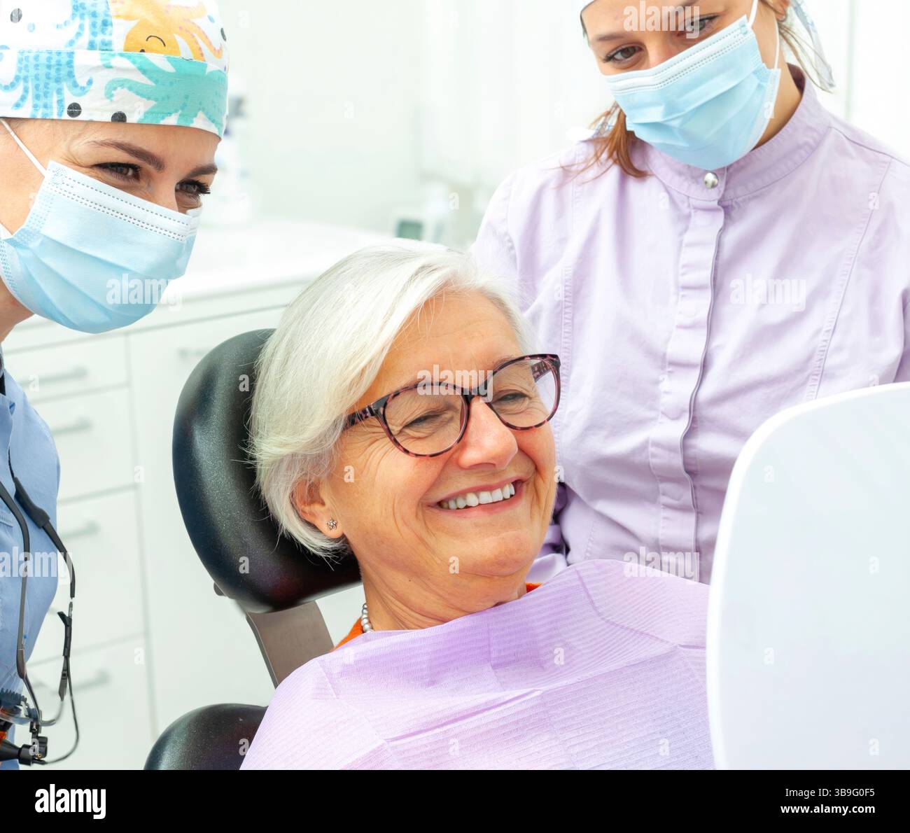 Dentists assisting a senior woman as she admires her smile in the ...