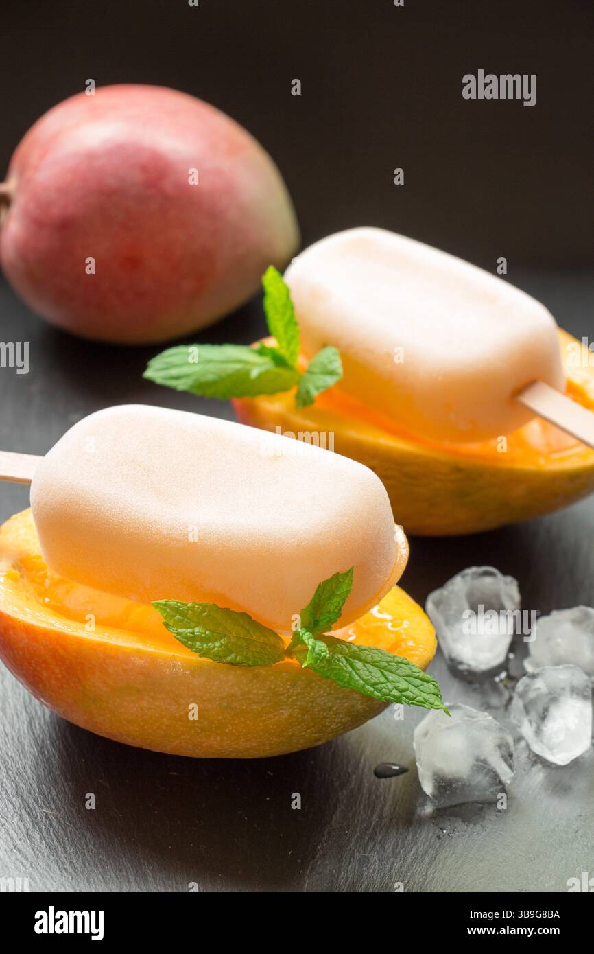 Mango sorbet ice cream on half cutted mango fruit behind mango near ice ...