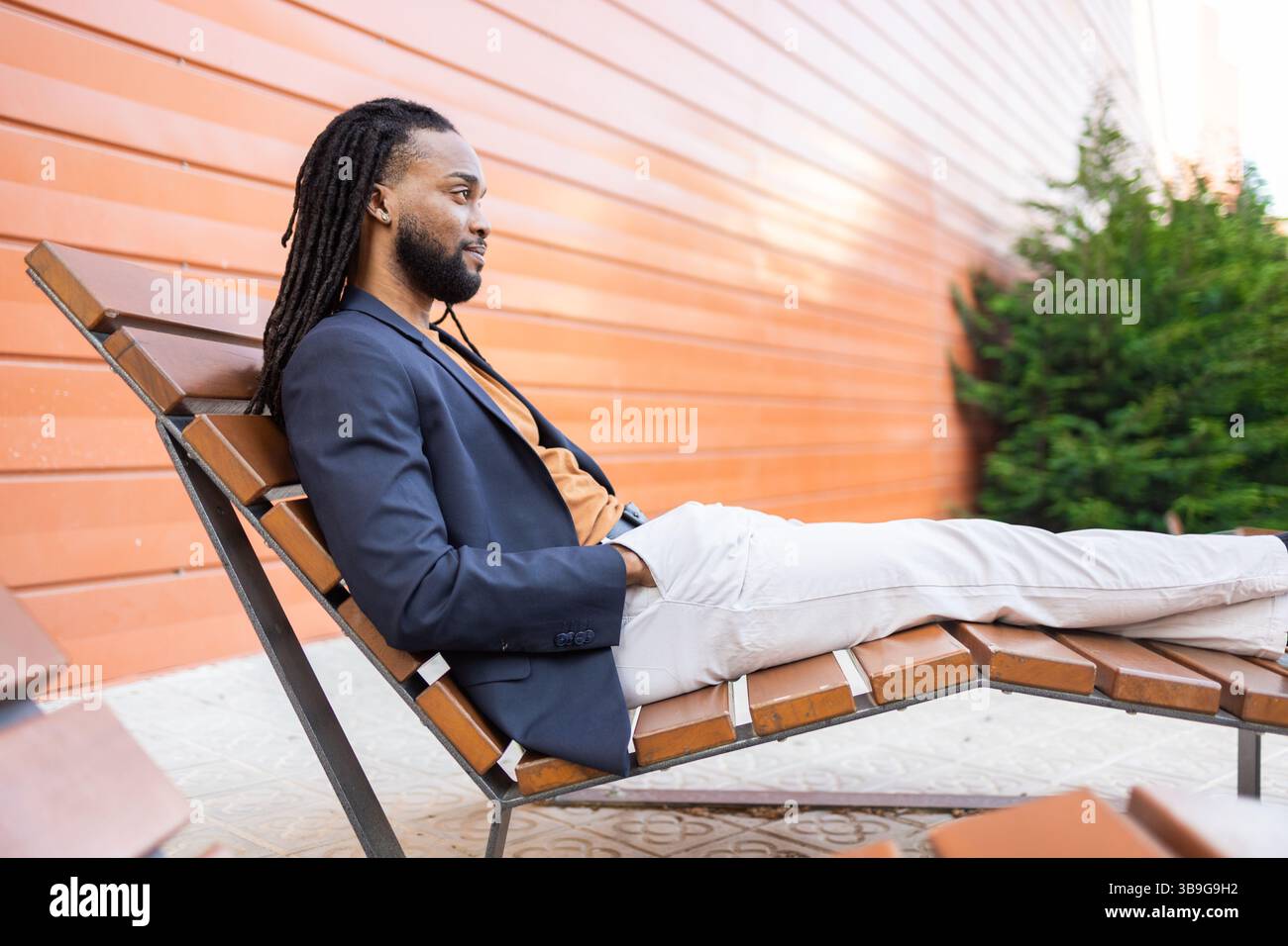 A business man with relaxed posture sits on a modern wooden lounge ...