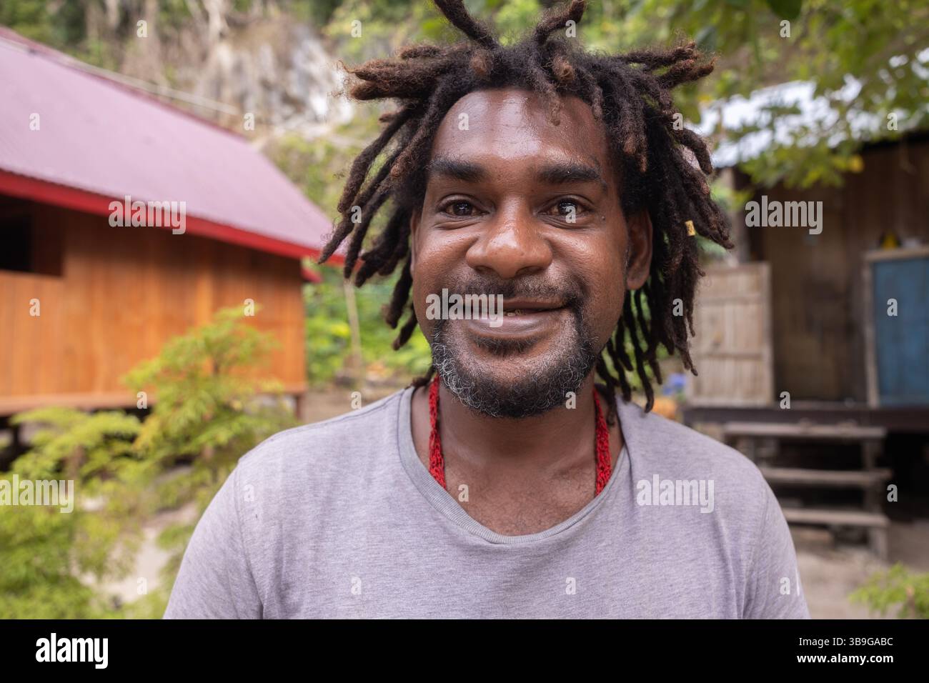 A cheerful native man with dreadlocks in front of a traditional house ...