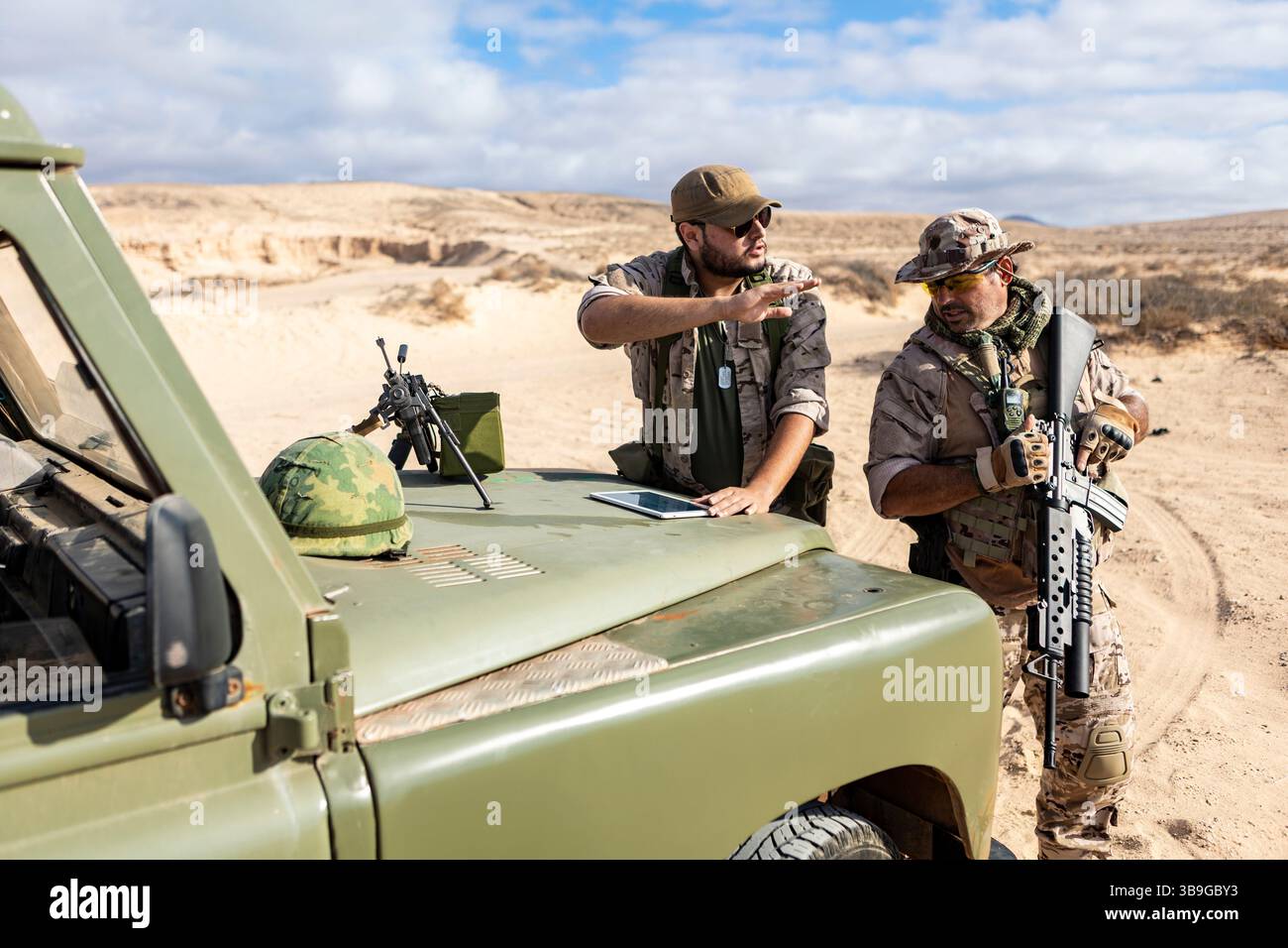 Two military soldiers in tactical gear discuss strategy near an off ...