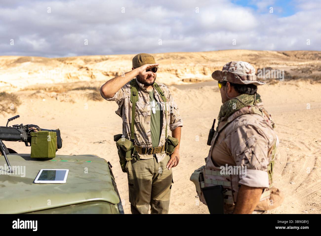 Two military personnel in desert camouflage gear communicate beside a ...