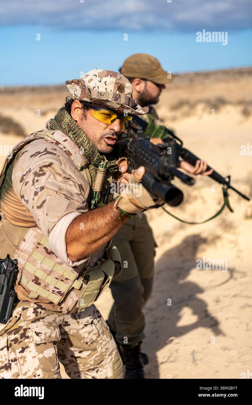 Two soldiers in camouflage gear aim rifles in a desert landscape ...
