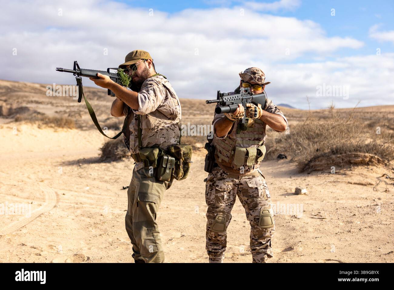 Two soldiers in tactical gear engage in a military exercise in a desert ...