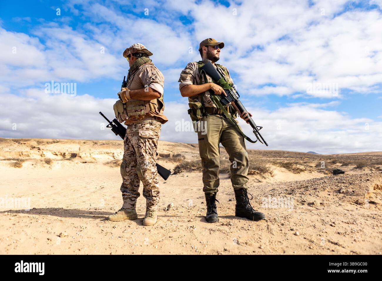 Two soldiers equipped with tactical gear and rifles stand back to back ...