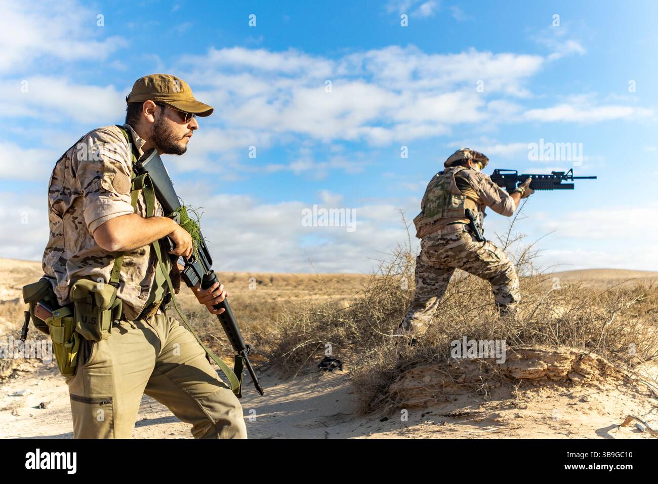 Two armed soldiers in desert terrain, wearing tactical gear and ...