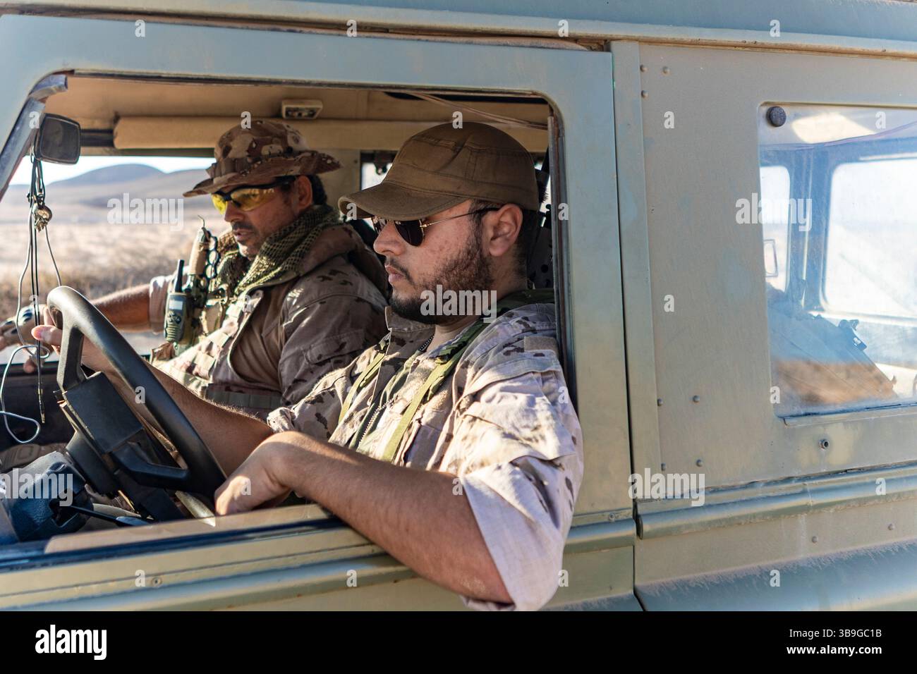 Two military soldiers wearing tactical gear sit inside an armored ...