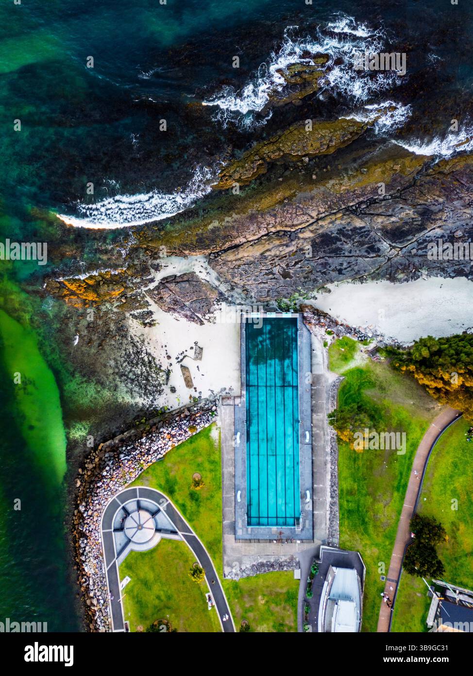 A stunning aerial view captures a seaside pool adjacent to a rocky shore with waves crashing ...