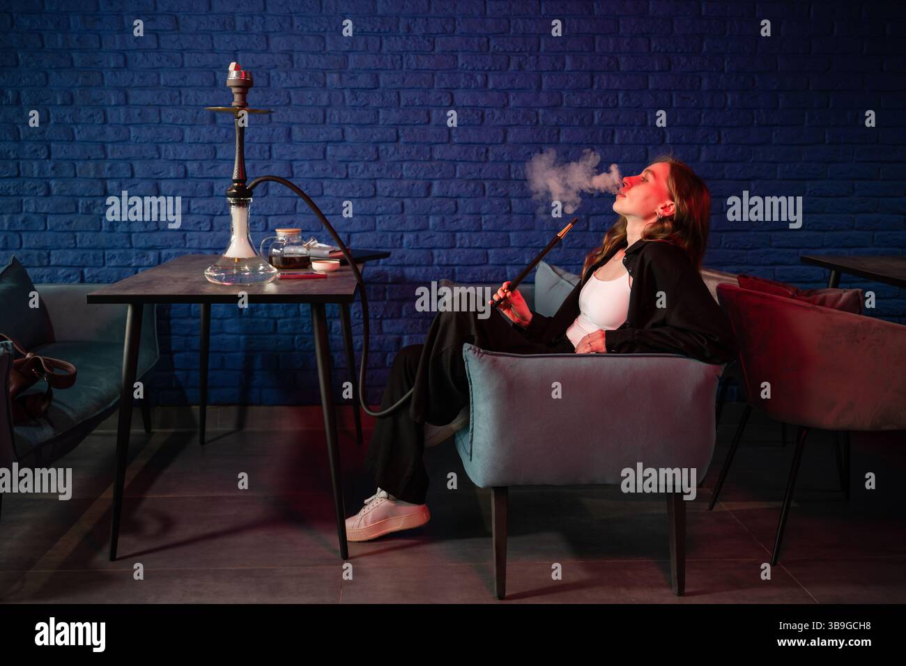 A young woman lounges comfortably in a modern hookah bar, enjoying a ...