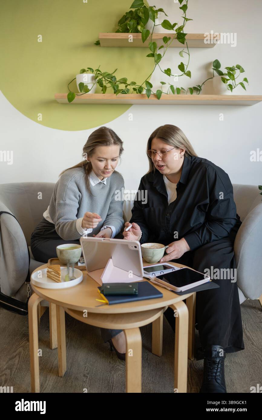 Two women engage in a collaborative discussion at a cozy cafe, using a ...