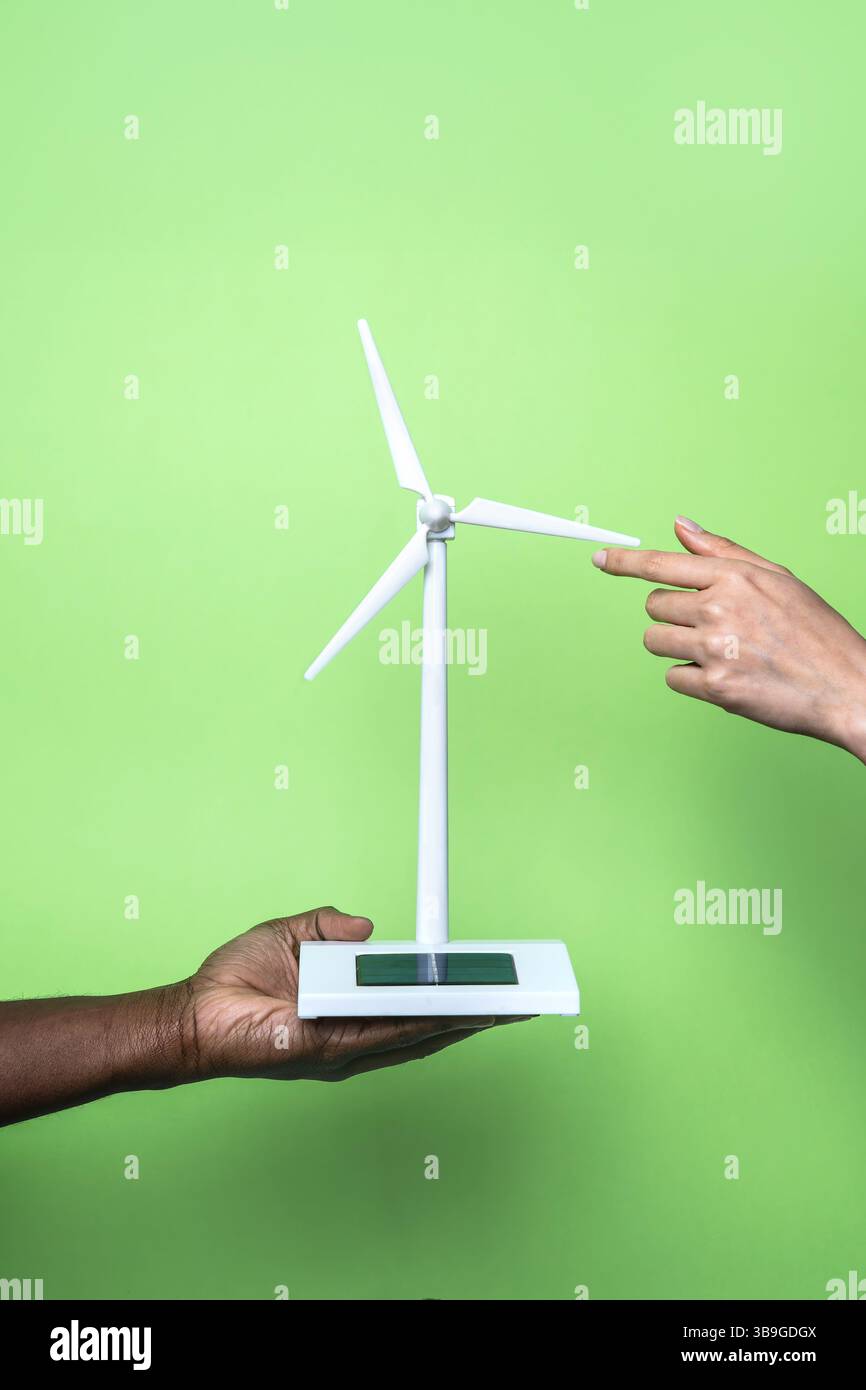 Close-up of two hands holding a small wind turbine model against a ...