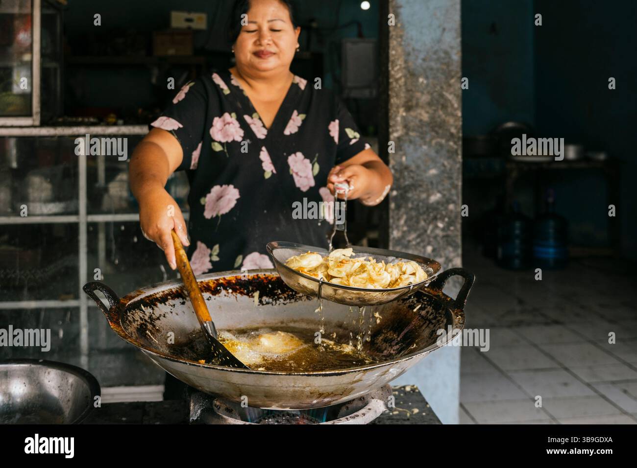 Woman expertly fries in hot oil using a large wok. The scene captures a ...