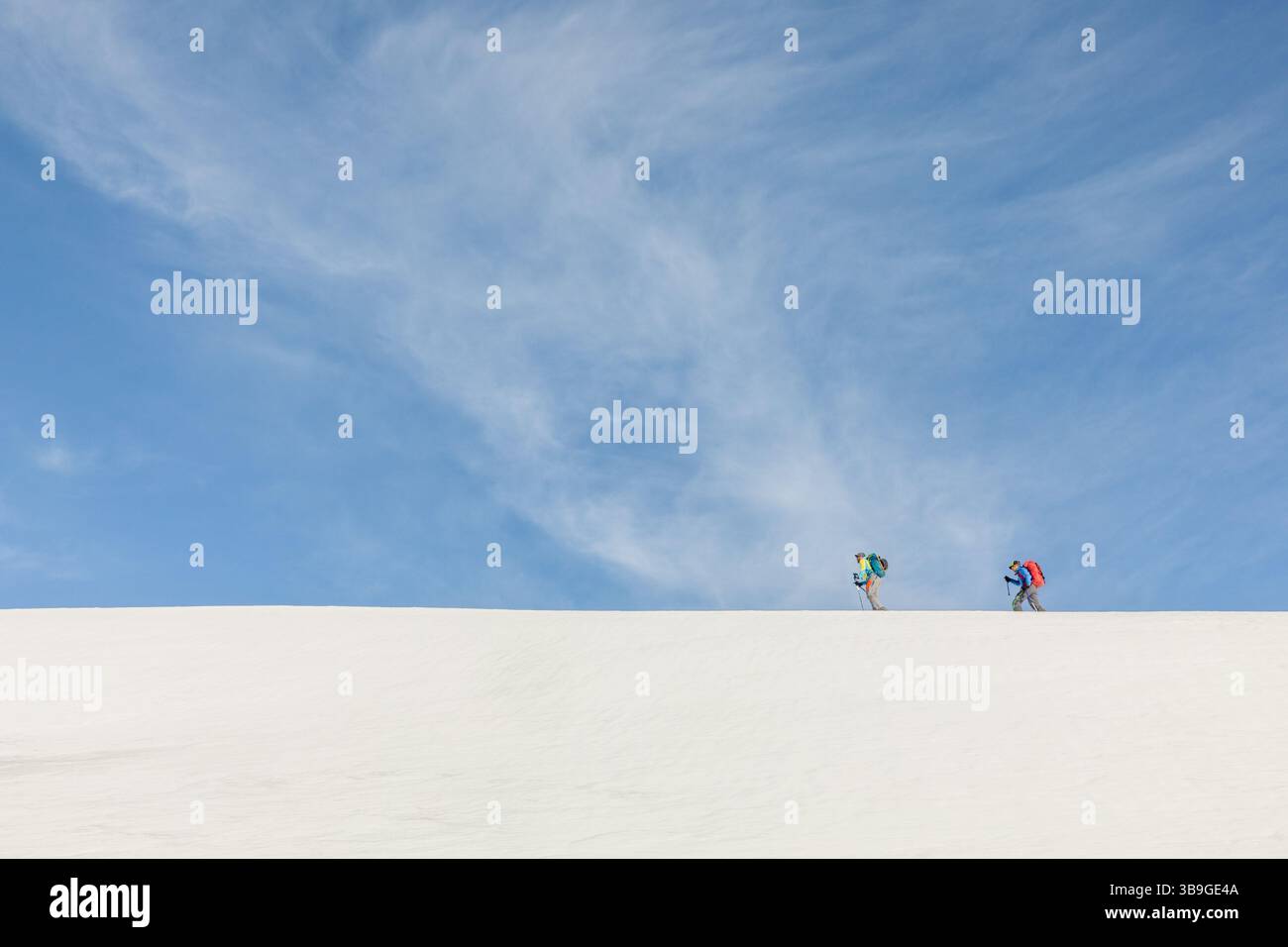 Two ski tourers traverse a pristine, snowy expanse beneath a clear blue ...
