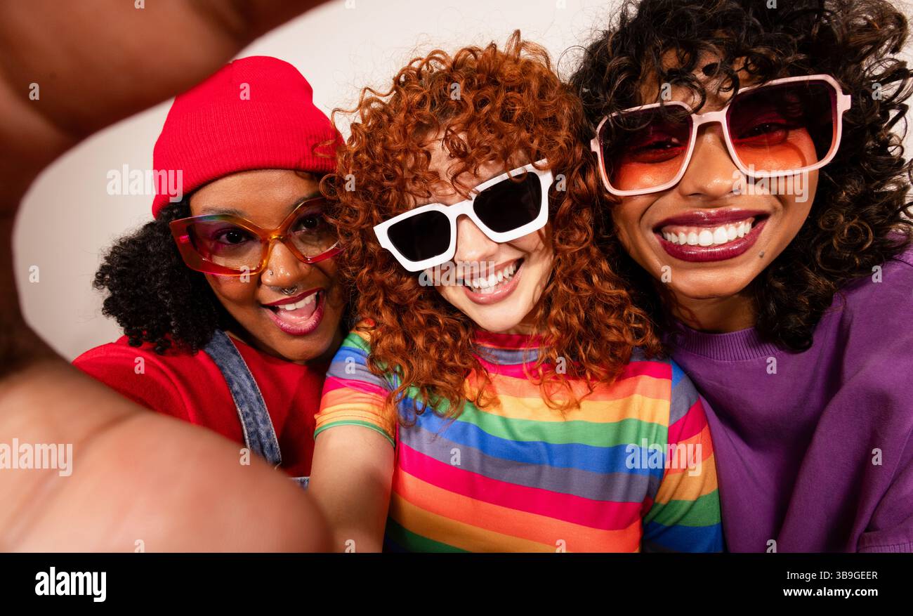 Three multiethnic women in vibrant outfits and sunglasses joyfully pose ...