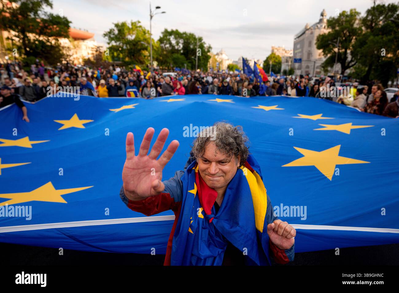 A man with Romanian and European Union flags draped over his shoulders ...