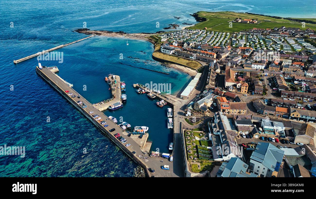 Aerial view of a coastal town with a harbor, breakwater, boats, houses ...