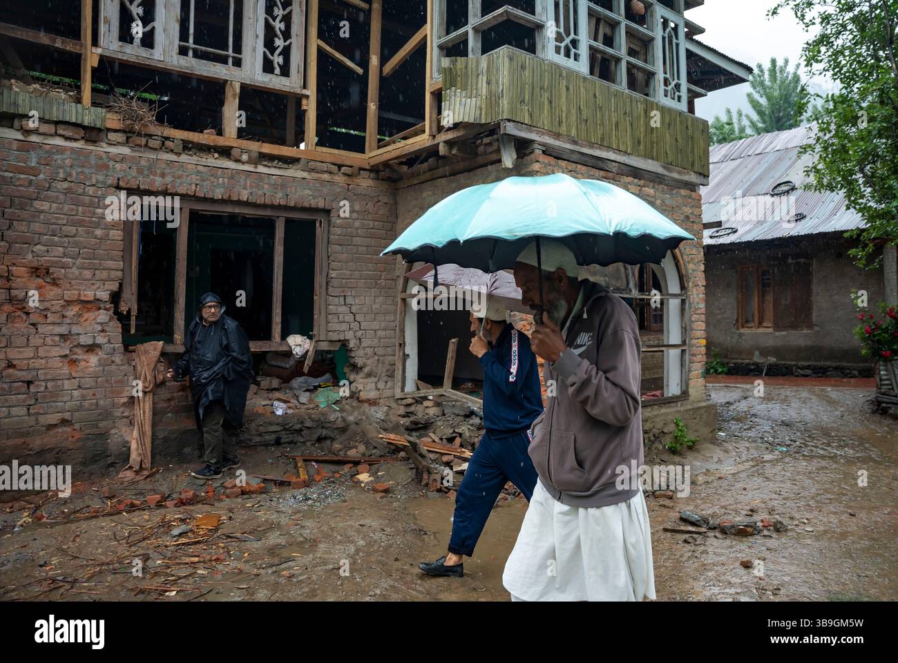 Indian villagers walk with an umbrella in front of a house damaged by ...