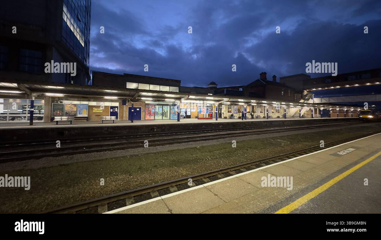 A railway station platform at dusk, showing train tracks, buildings ...