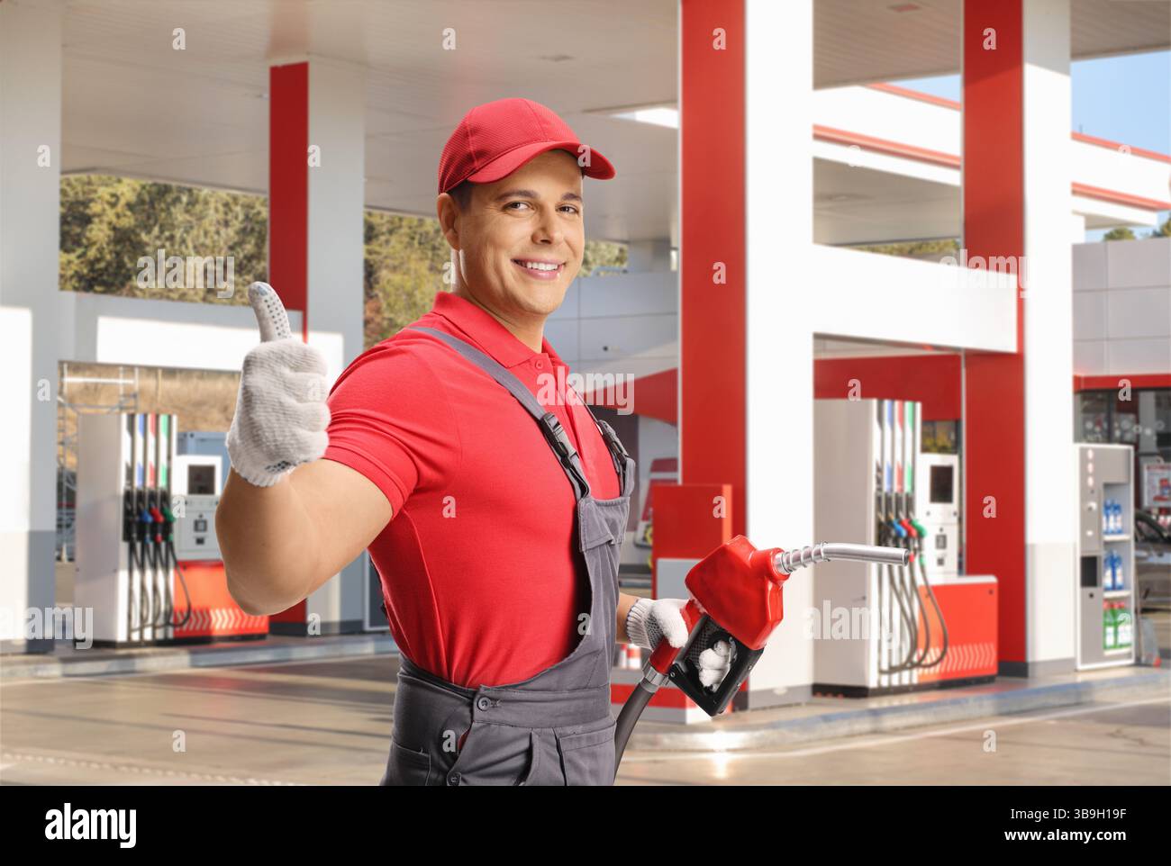 Petrol station worker holding a petrol gun and gesturing thumbs up ...