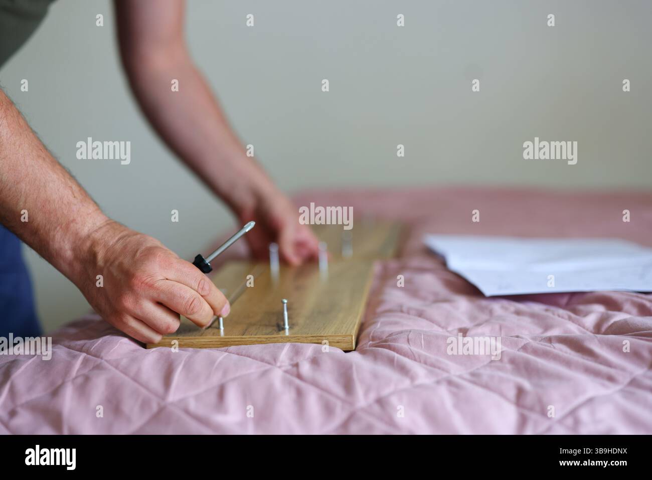 man hand using manual screwdriver and screwing screw in board of drawer ...