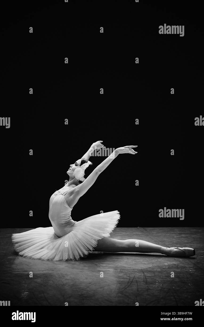 Ballet dancer in white tutu performing graceful split pose on dark ...