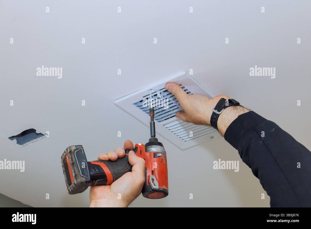 Carpenter is fixing an air vent cover in ceiling with drill in ...