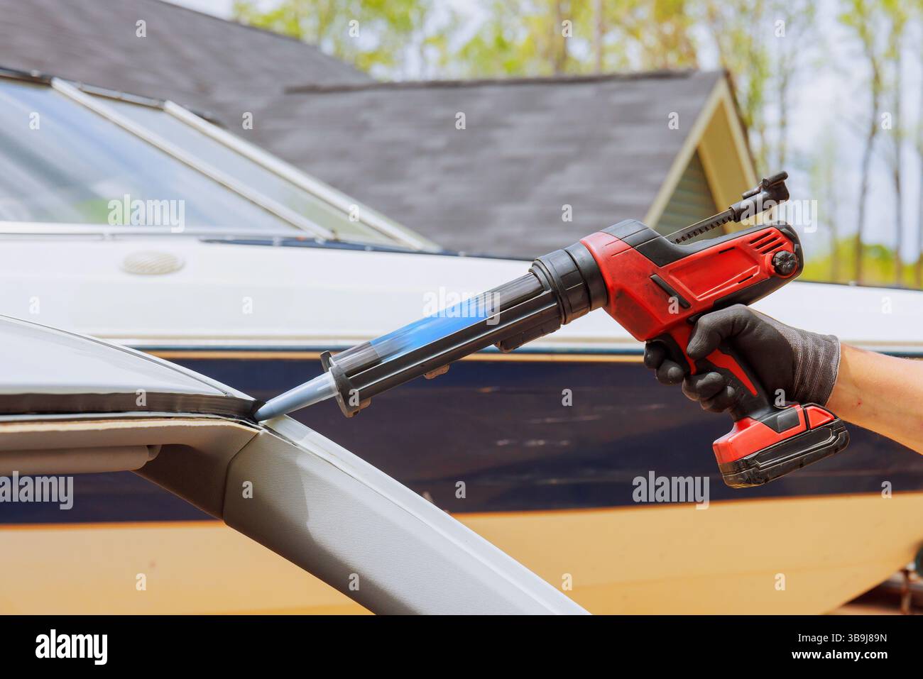 Worker is sealing windshield edge with caulking gun while repair ...