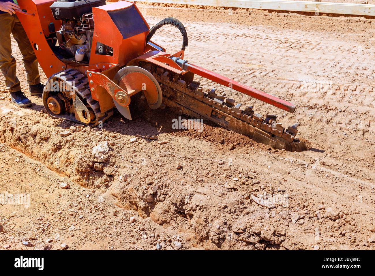 Worker uses trencher to dig seam for underground utilities at ...