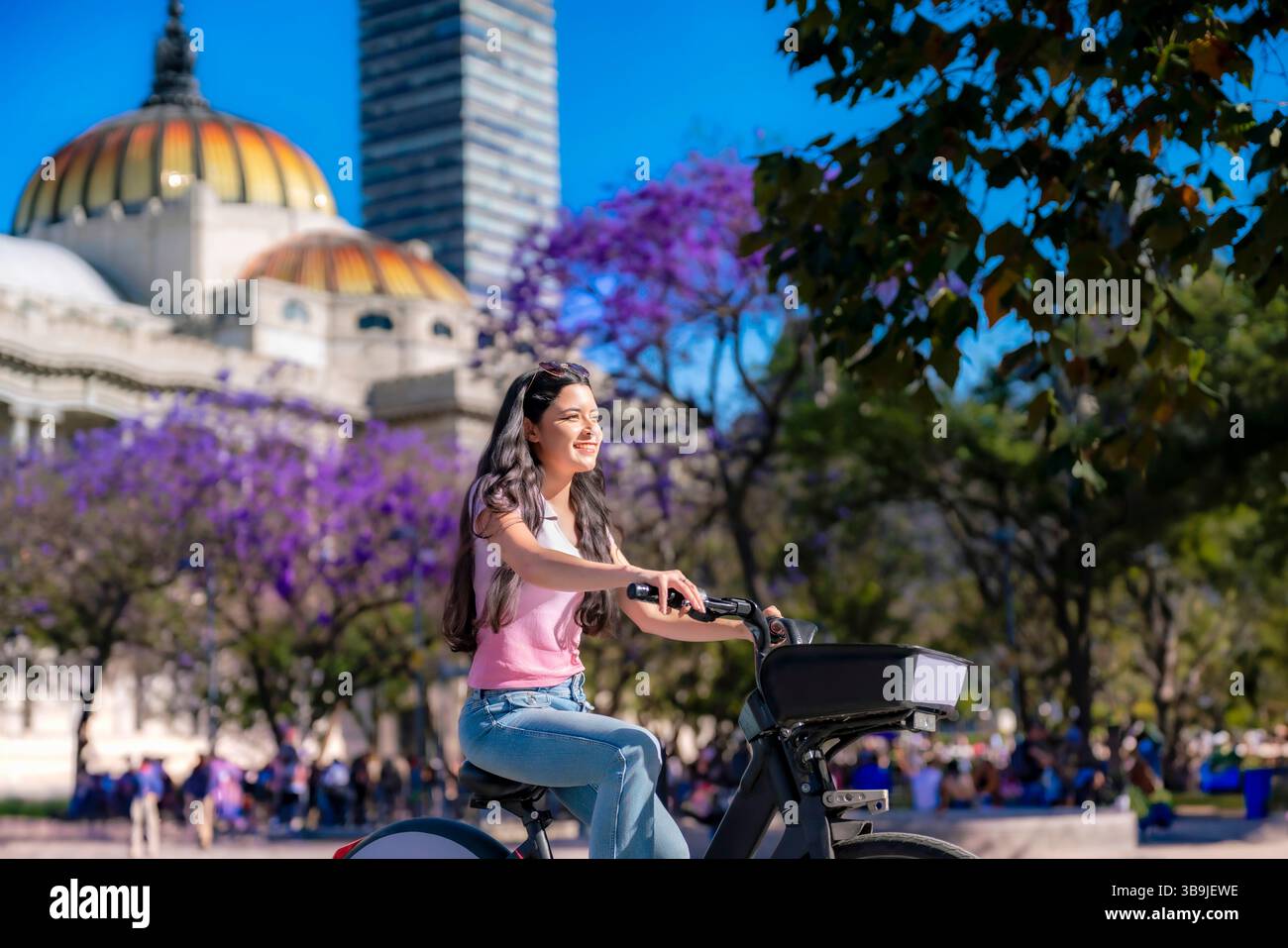 Young latina woman smiling while cycling past Bellas Artes and Torre ...
