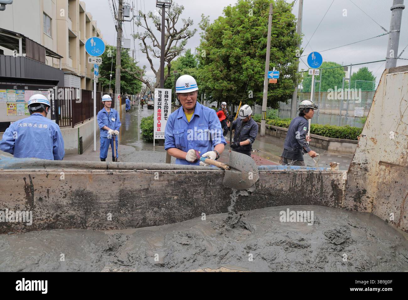 Workers from the Osaka City Water Bureau shovel mud from a flooded road ...