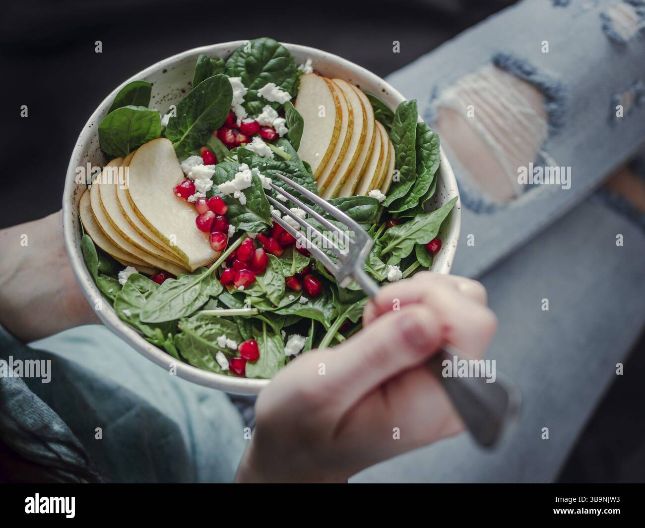 Woman in jeans holding vegan salad bowl with spinach, pear, pomegranate ...