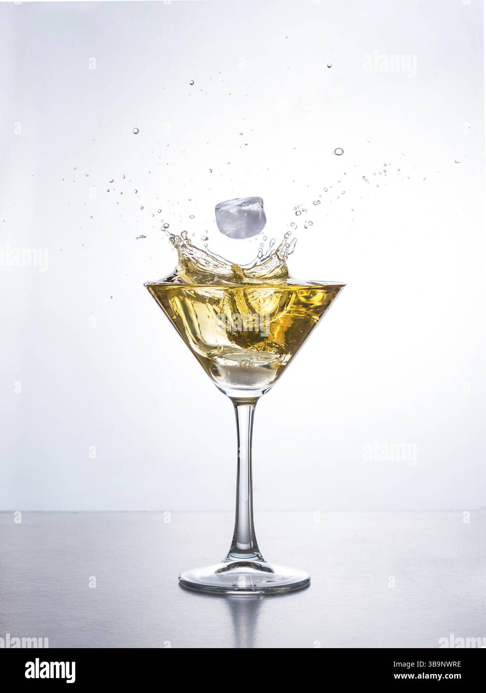 Yellow cocktail in martini glass with ice cube splashing into liquid ...